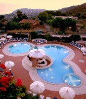 Área de piscina com duas piscinas circulares, espreguiçadeiras, guarda-sóis e vista para a paisagem ao redor.