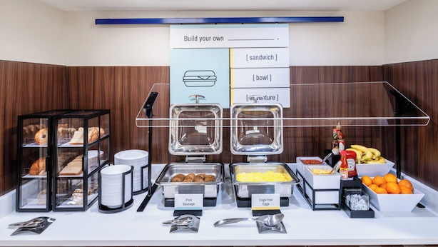 Buffet com seções de alimentos identificadas, incluindo linguiça de porco e ovos de galinhas criadas soltas.