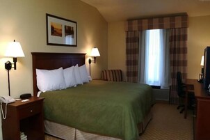 Quarto de hotel com uma cama grande, duas luminárias de cabeceira, uma mesa de trabalho com cadeira, um telefone e uma janela com cortinas.