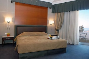 Quarto de hotel com uma cama grande, duas luminárias de cabeceira, uma pequena mesa com bandeja de café da manhã e vista para o exterior.