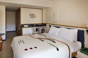 Quarto de hotel com cama, secretária, cadeira, máquina de café e quadro na parede.
