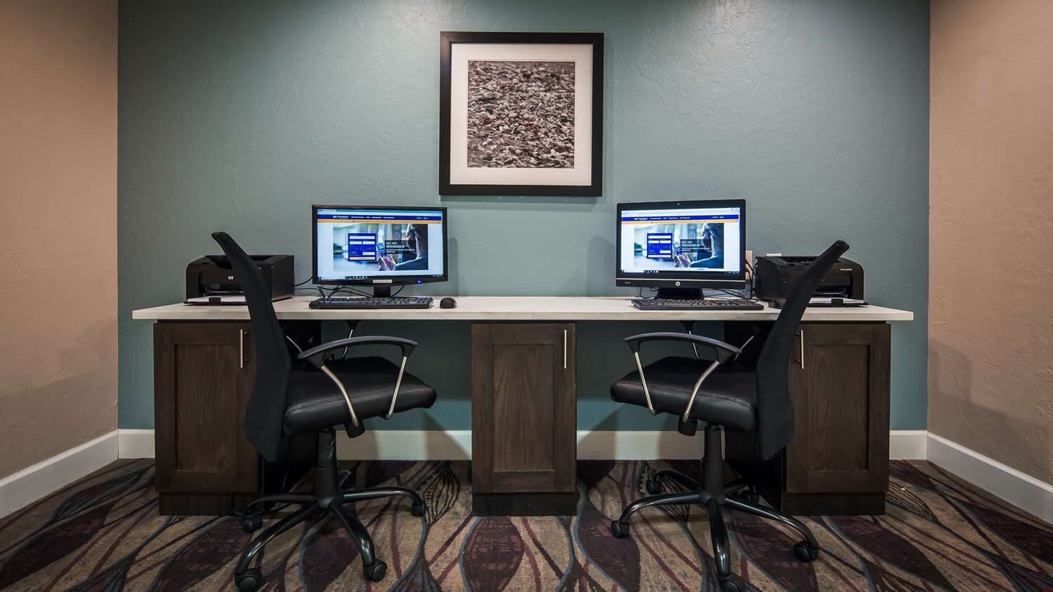 Uma sala de conferências com duas mesas, cada uma com um computador e uma impressora, e duas cadeiras de escritório.