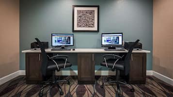 Uma sala de conferências com duas mesas, cada uma com um computador e uma impressora, e duas cadeiras de escritório.