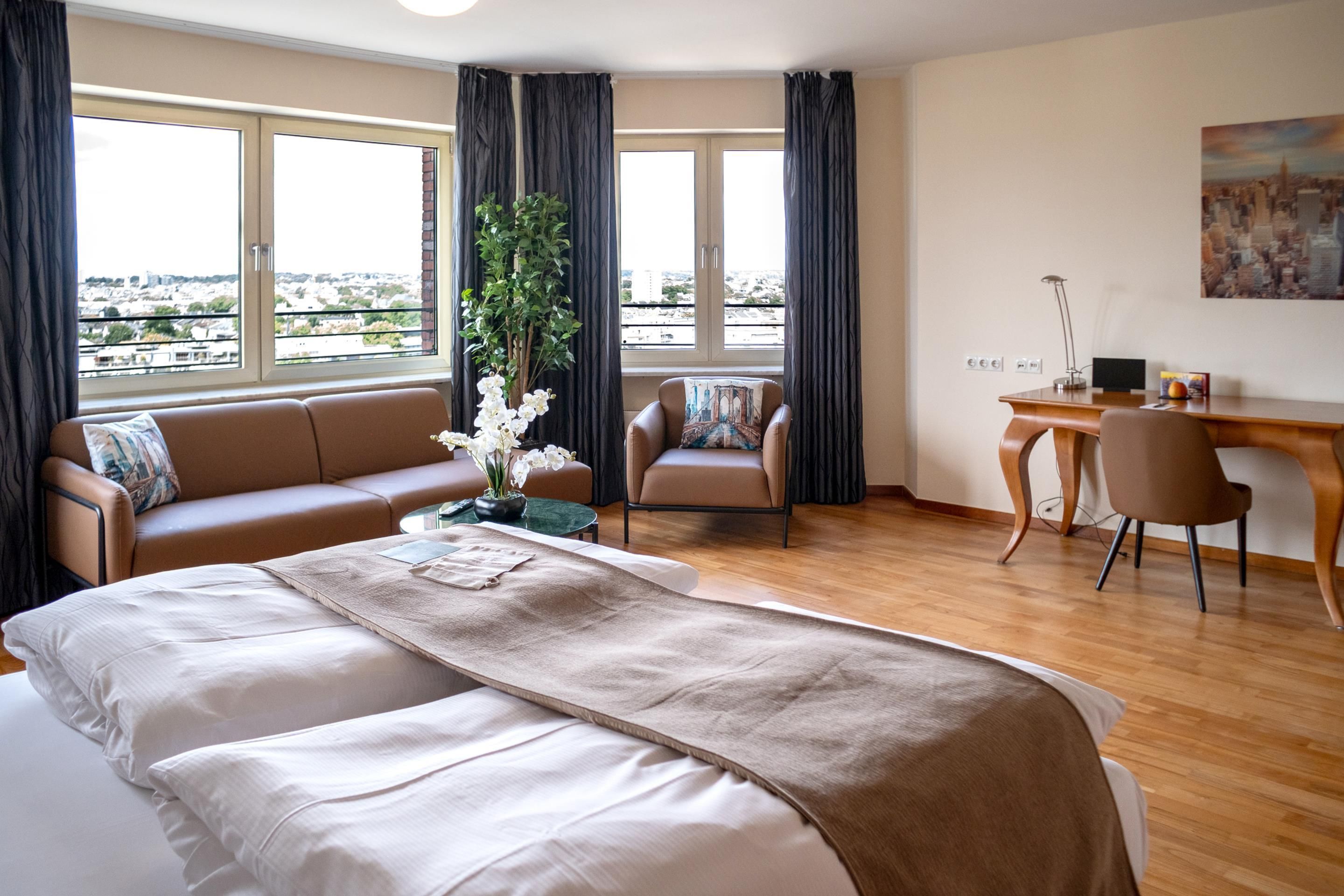 Quarto de hotel com cama, sofá, escrivaninha e vista para a cidade.