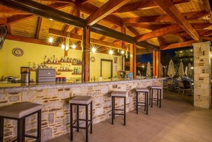 Uma área de bar com paredes de pedra, vigas de madeira e banquetas.
