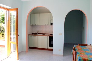 Cozinha com armários brancos, pia e mesa de jantar com toalha de mesa colorida.