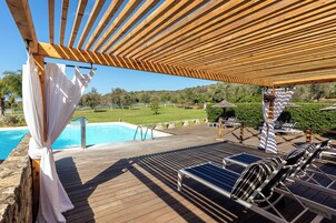 Um deck de madeira com piscina, cadeiras de descanso e um pergolado para sombra.