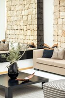 Uma sala de estar moderna com parede de pedra, sofá, mesa de centro com vaso e objeto decorativo, e um tapete estampado.