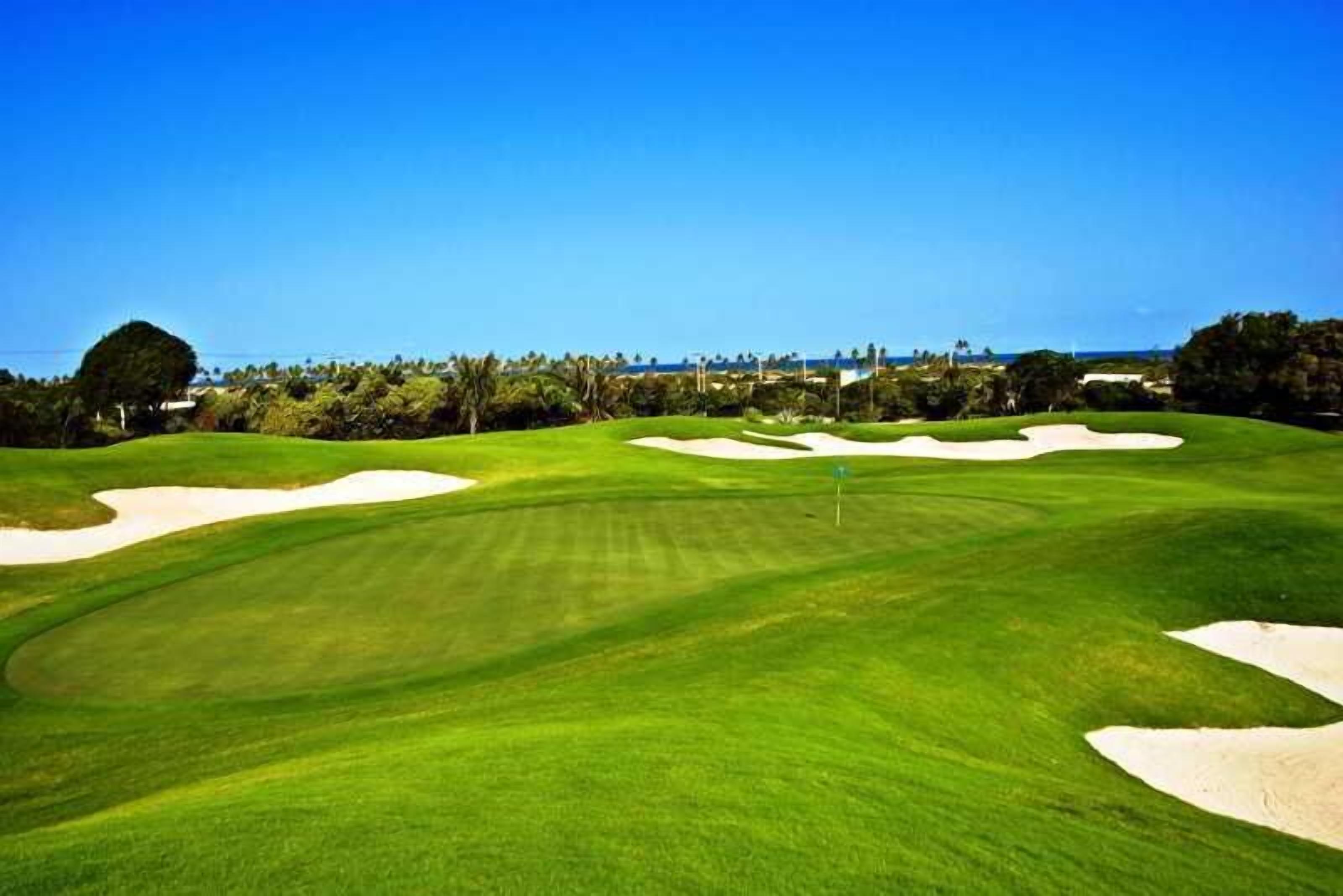 Um campo de golfe com bunkers de areia, haste de sinalização e um céu azul límpido.