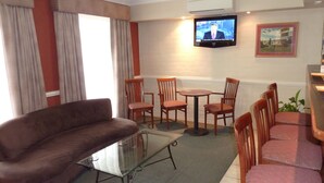Uma sala de estar com sofá, mesa de centro de vidro, televisão na parede e um espaço de jantar com cadeiras e mesa de madeira.
