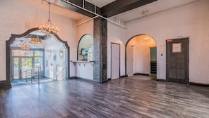 Um interior amplo com piso de madeira, um candelabro e uma escada que dá acesso a uma área externa.