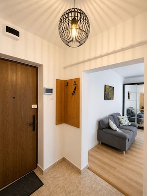 Um interior moderno com porta de madeira, um porta-roupas fixado na parede, um sofá cinzento e um lustre.