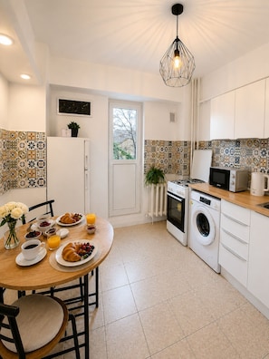 Uma cozinha moderna com armários brancos, uma mesa de jantar com café da manhã, máquina de lavar e microondas.