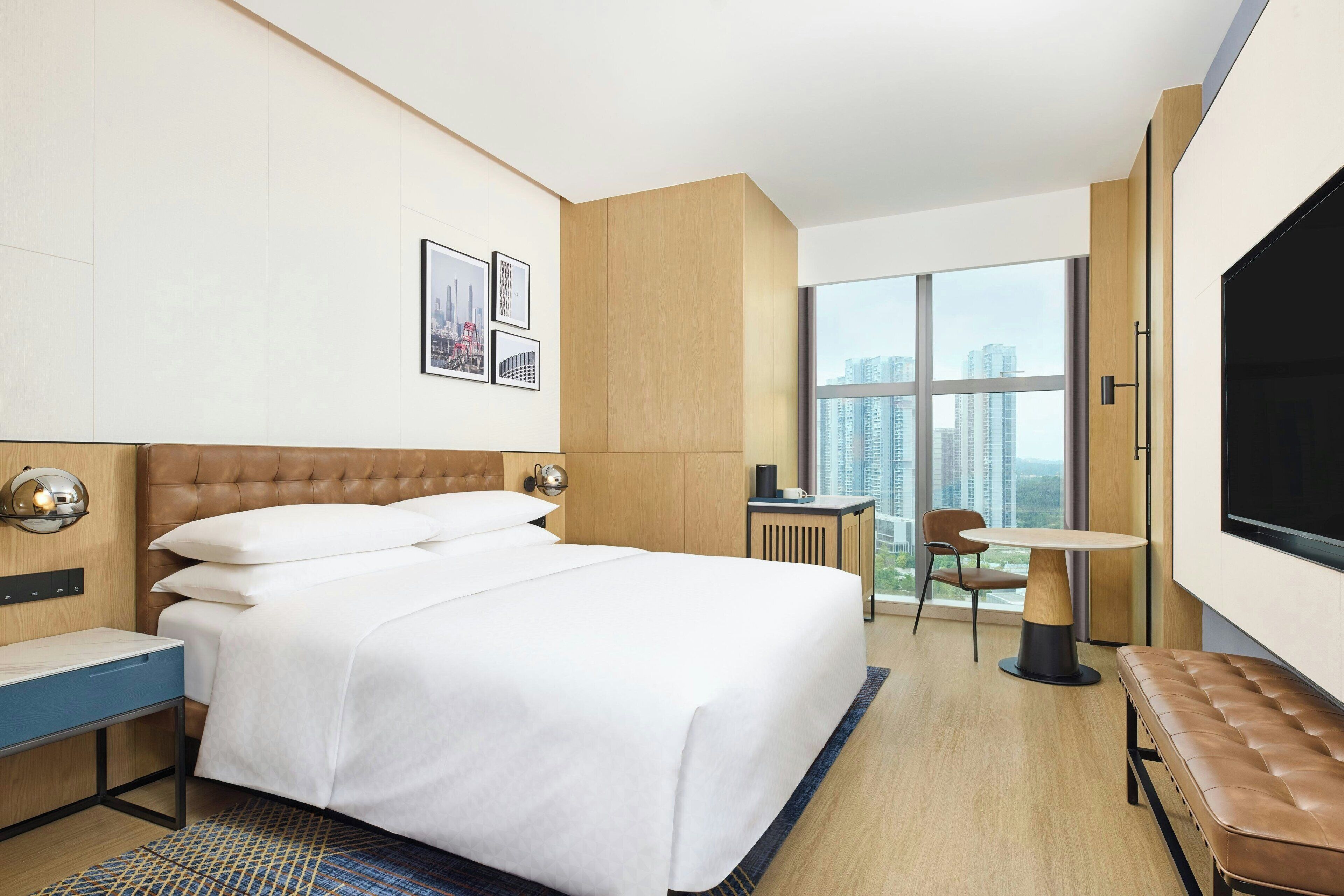 Quarto de hotel com uma cama grande, escrivaninha, cadeira, banquinho e televisão.