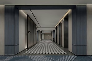Um corredor moderno de hotel com piso estampado, painéis de madeira escura e um lustre central.