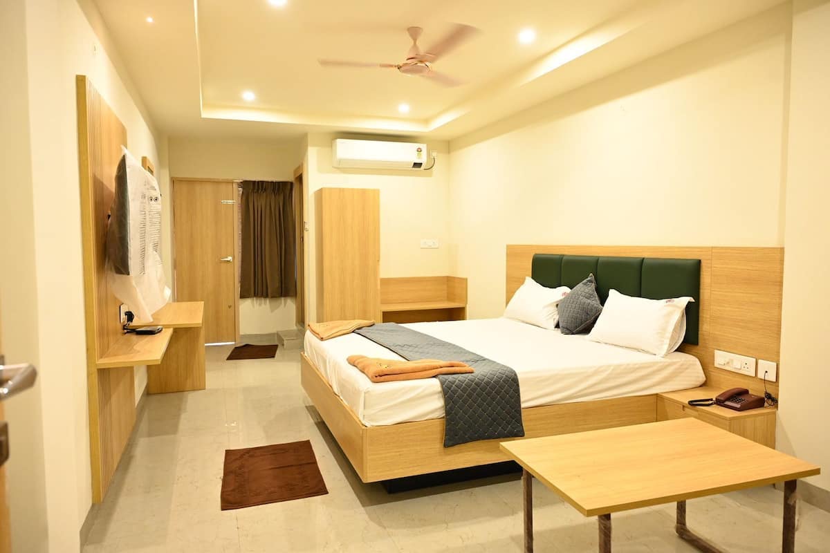 Quarto de hotel com cama, mesa de cabeceira, escrivaninha, ar condicionado e ventoinha no teto.