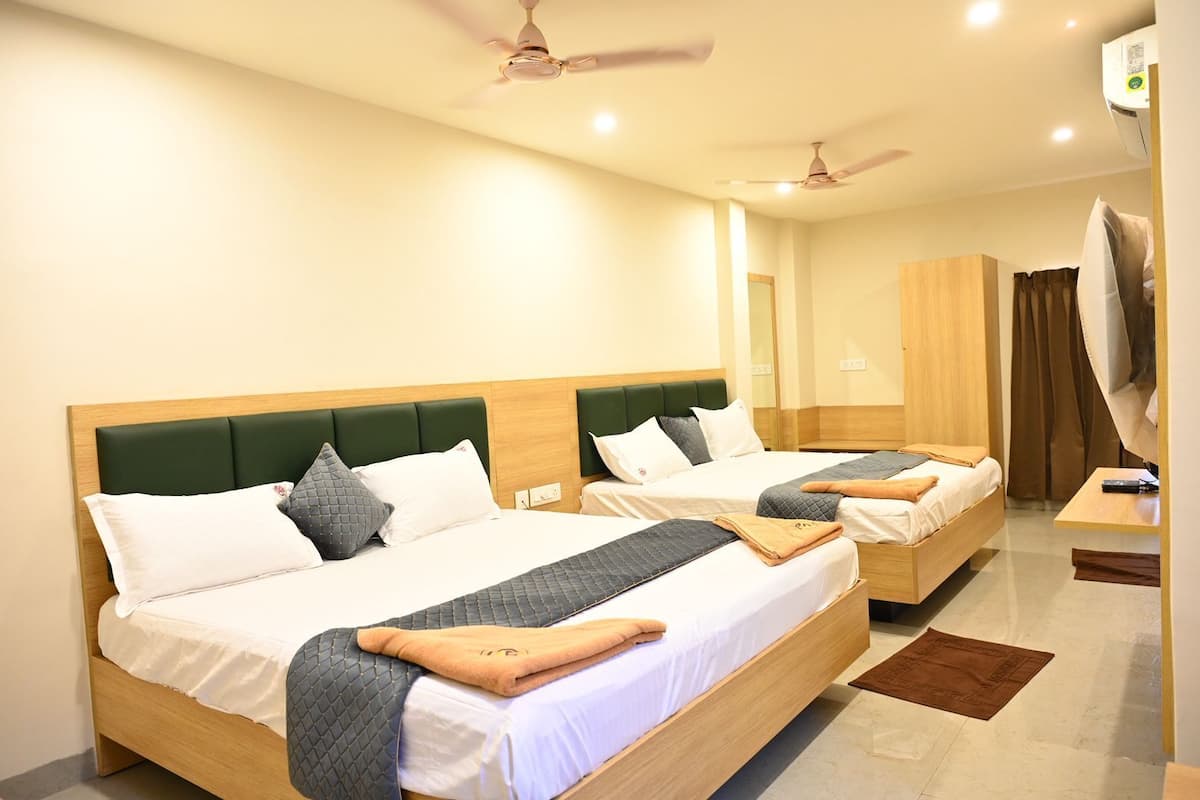 Quarto de hotel com duas camas, televisão, guarda-roupa e ventoinha no teto.