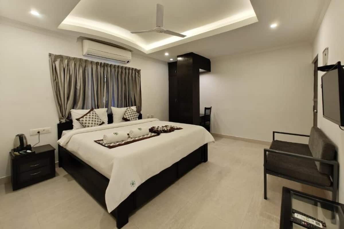 Quarto moderno com cama, mesas de cabeceira, televisão e ventilador de teto.