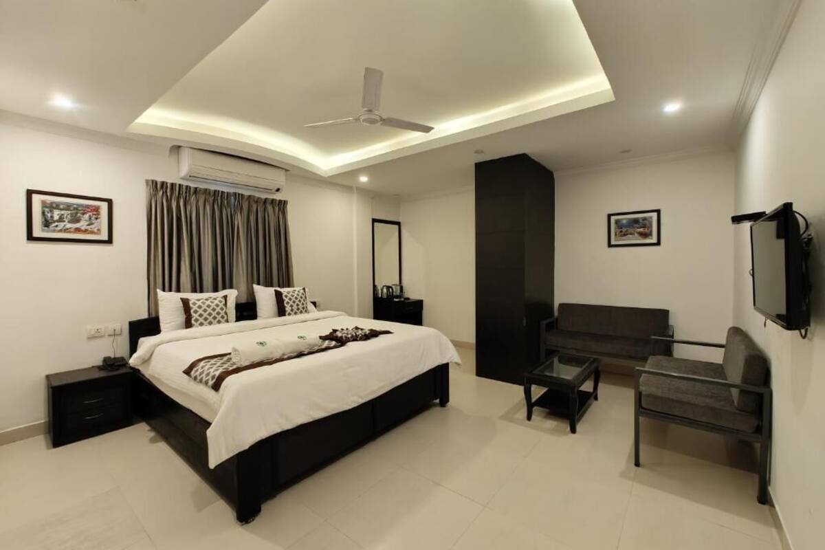 Um quarto moderno com cama, mesas de cabeceira, escrivaninha, cadeira, ventilador de teto e ar condicionado.