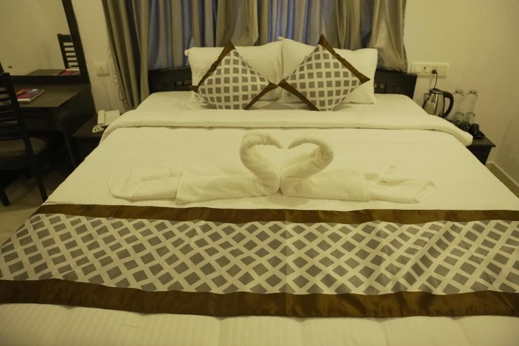 Quarto de hotel com uma cama bem arrumada, uma escrivaninha com cadeira e uma mesa de cabeceira com abajur.