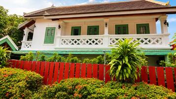 Um edifício tradicional com varanda, persianas verdes e uma cerca vermelha.