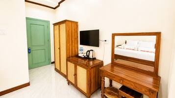 Quarto de hotel com uma cama, televisão, armário de madeira, cesto de vime e uma porta verde.