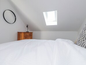 Quarto com cama, mesa de cabeceira de madeira, luminária de mesa, janela e decoração circular na parede.