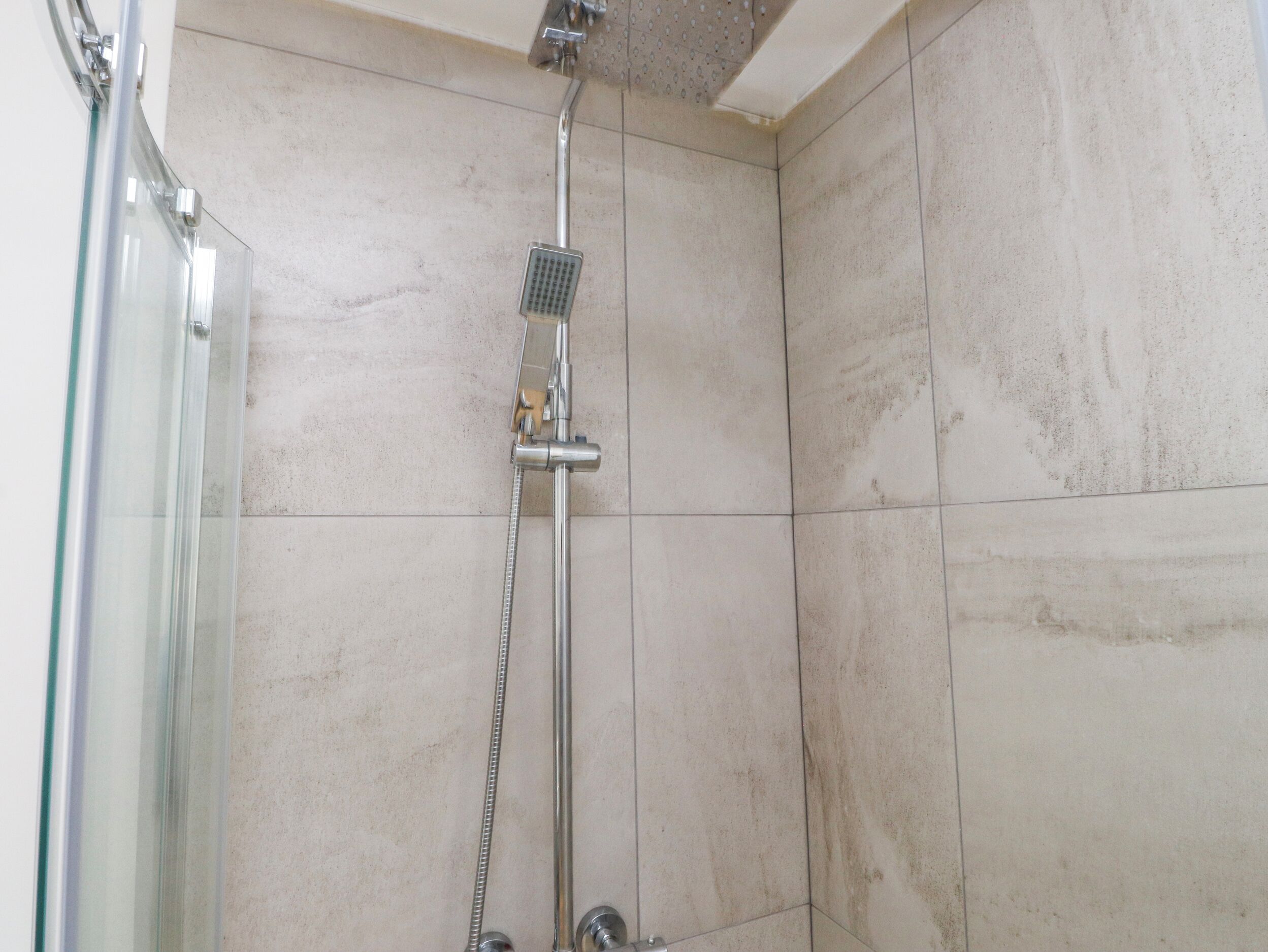 Chuveiro com box de vidro, chuveiro manual e torneira fixada na parede.