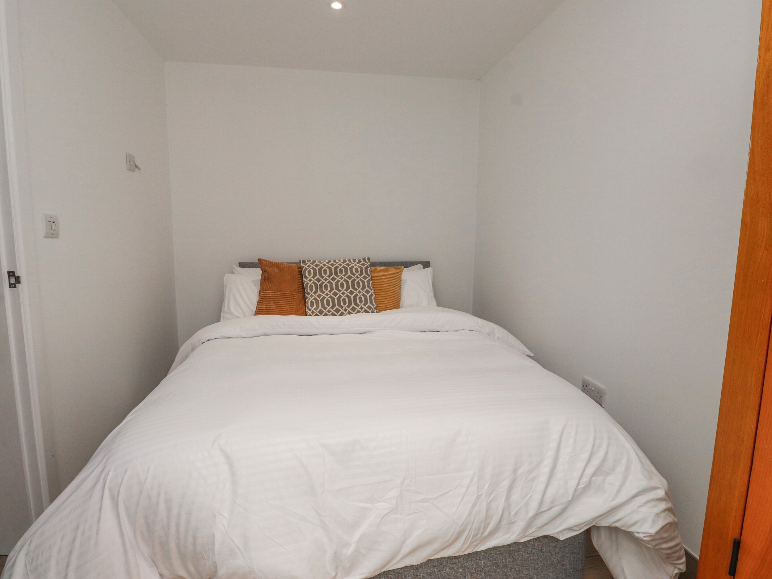 Uma cama de solteiro com edredom branco, almofada decorativa estampada e almofada marrom.