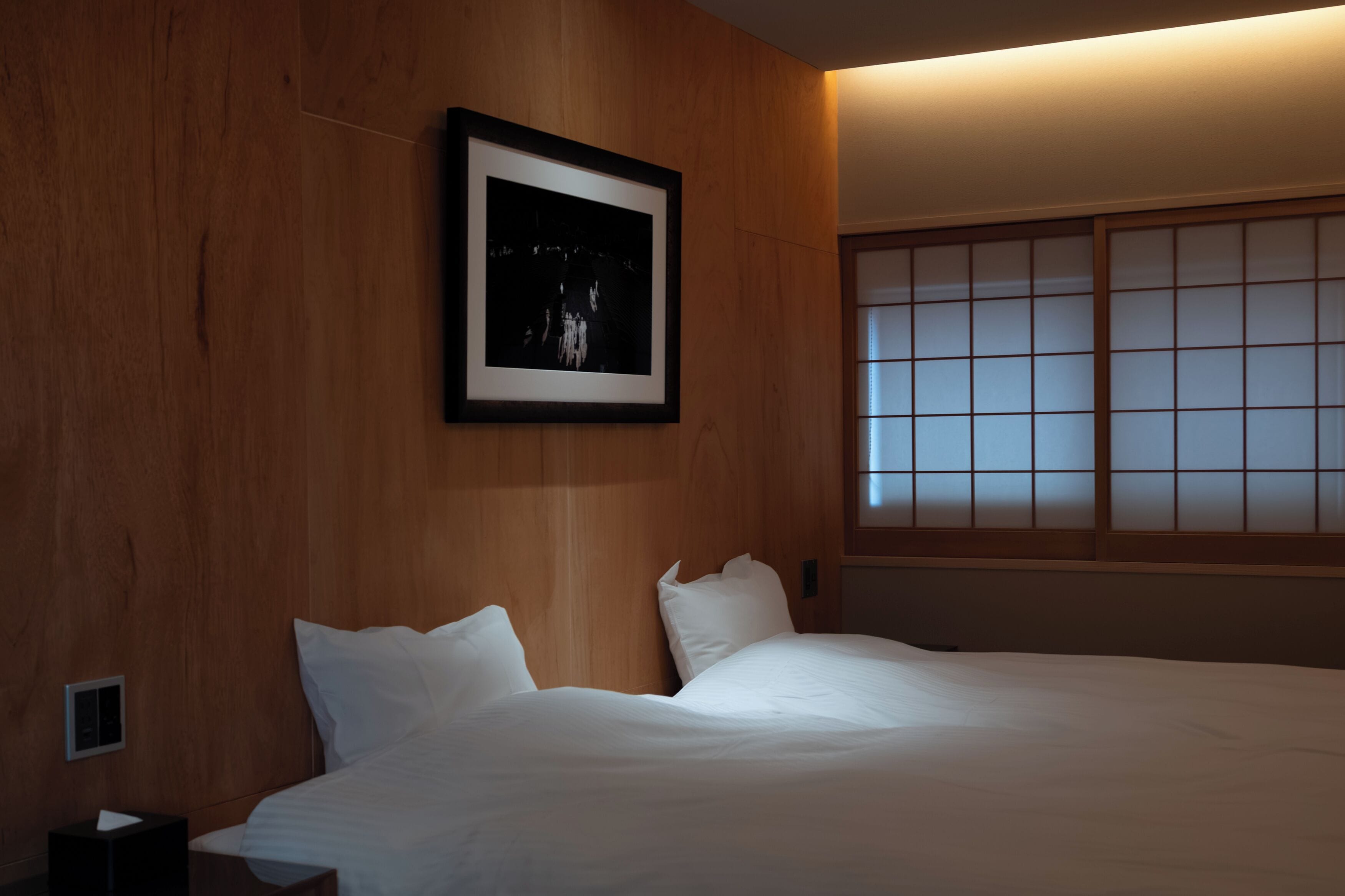 Quarto de hotel com uma cama, mesa de cabeceira, quadro na parede e janela com vista.