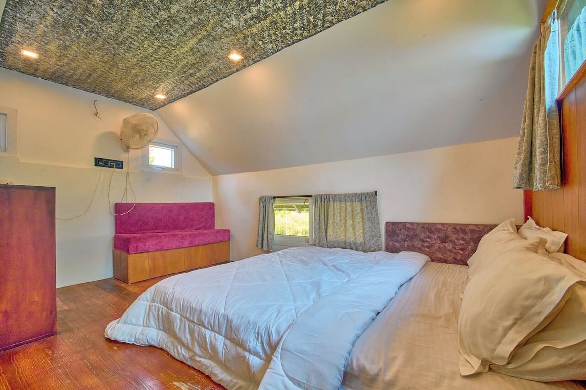 Um quarto com cama, um banco, uma janela e um ventilador de teto.