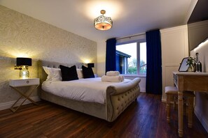 Quarto com cama, abajures, janela com cortinas, escrivaninha de madeira com espelho e um vaso com flores.