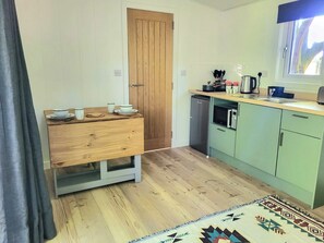 Uma cozinha compacta com uma mesa de madeira, micro-ondas, frigorífico e janela com vista.