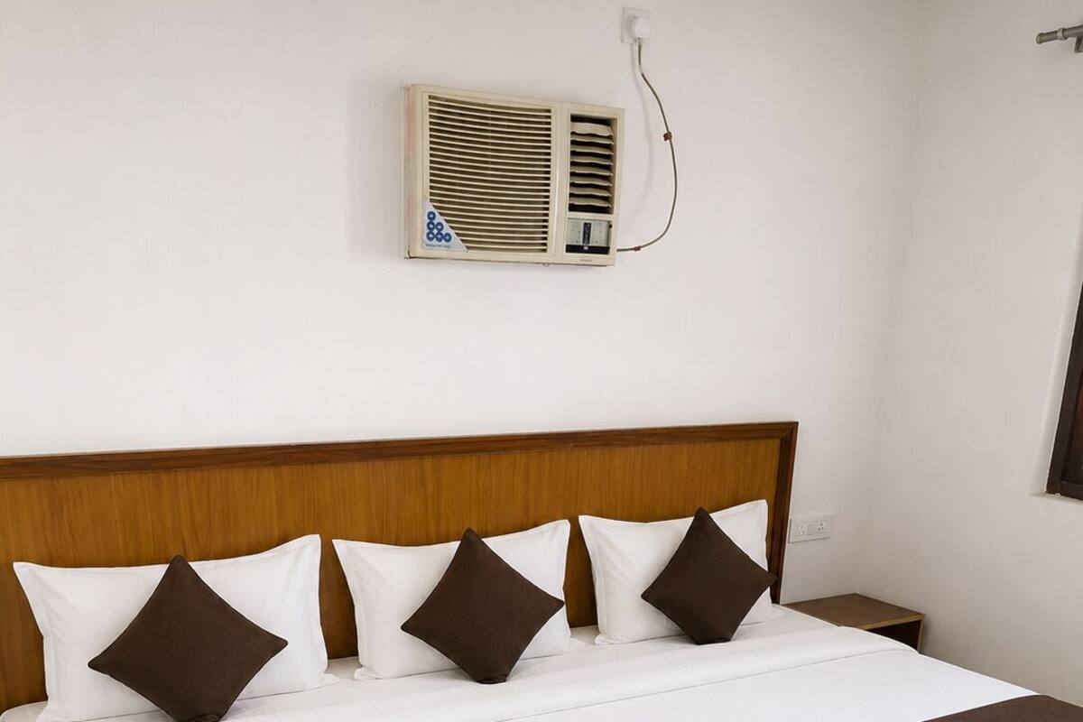 Uma cama com cabeceira de madeira, roupa de cama branca e castanha, e um ar condicionado fixado na parede.