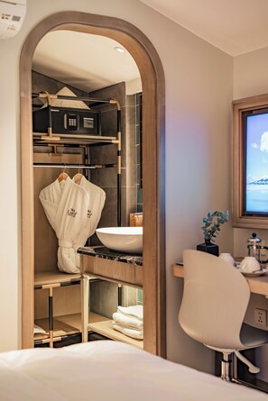 Quarto de hotel com closet espaçoso, cama, escrivaninha com cadeira, pia e uma janela grande.