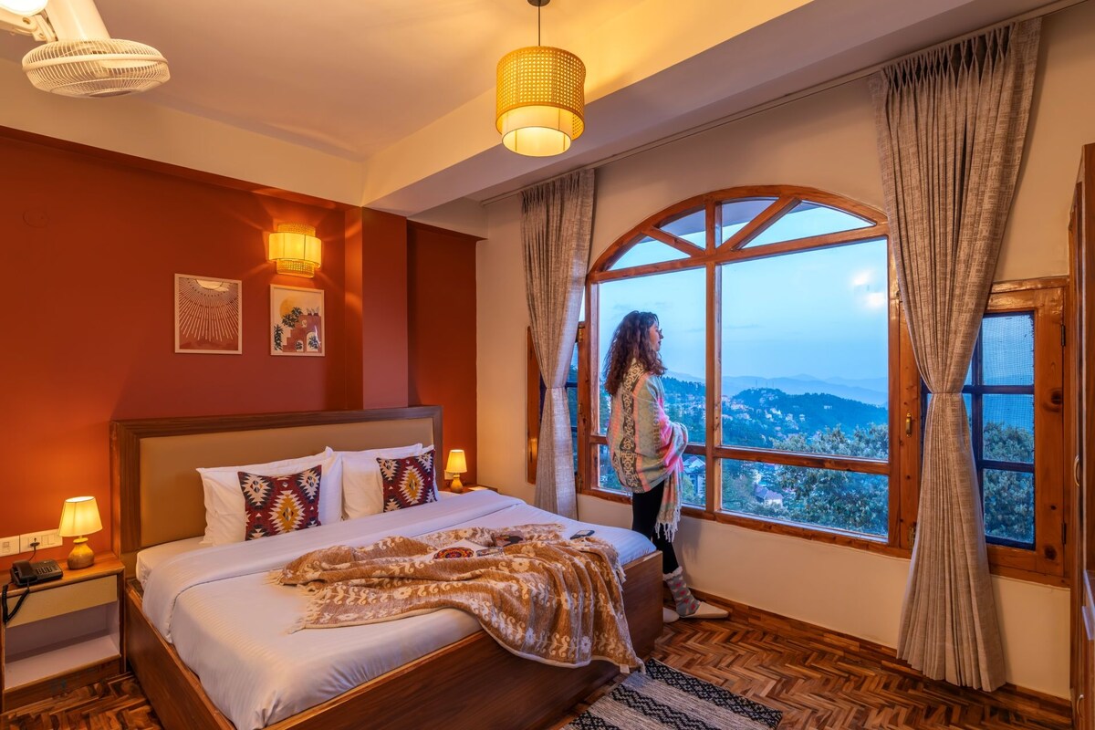 Quarto com uma cama grande, vista para uma paisagem montanhosa e piso de madeira.