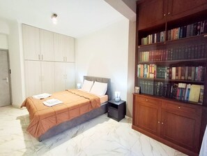 Quarto com cama, mesa de cabeceira, estante de livros e guarda-roupa.