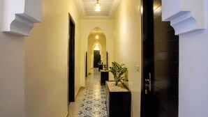Um corredor com piso de azulejos, uma porta preta e um luminário no teto.