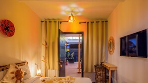 Quarto de hotel com cama, luminária de cabeceira, relógio na parede, televisão e vista para a área externa.