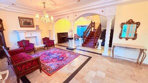 Uma sala de estar ampla com lareira, dois poltronas, um piano e uma escada que leva a um andar superior.