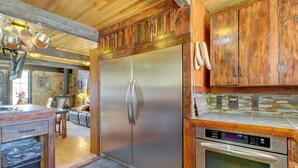 Uma cozinha com geladeira de aço inoxidável, armários de madeira, forno embutido e painel de parede de pedra.