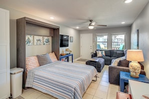 Quarto com cama, televisão, ventoinha no teto e vista para o exterior.