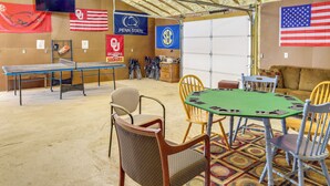 Um quarto com mesa de pingue-pongue, cadeiras, uma mesa verde e diversas bandeiras.