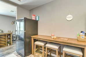Uma cozinha com geladeira de aço inoxidável, mesa de madeira e banquetas.