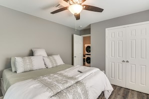 Quarto com cama, ventilador de teto, máquina de lavar ao fundo e uma porta branca.