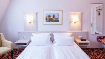 Quarto de hotel com duas camas, mesas de cabeceira, uma cadeira, um quadro emoldurado na parede e uma porta com um cabide.