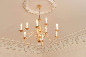 Um candelabro com várias lâmpadas que lembram velas, uma medalhão decorativa no teto e painéis florais na parede.