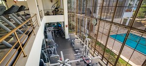 Ginásio com esteiras, máquinas de pesos e piscina visíveis através de um revestimento de vidro.
