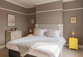 Quarto com cama, mesa de cabeceira, cômoda e um quadro na parede.