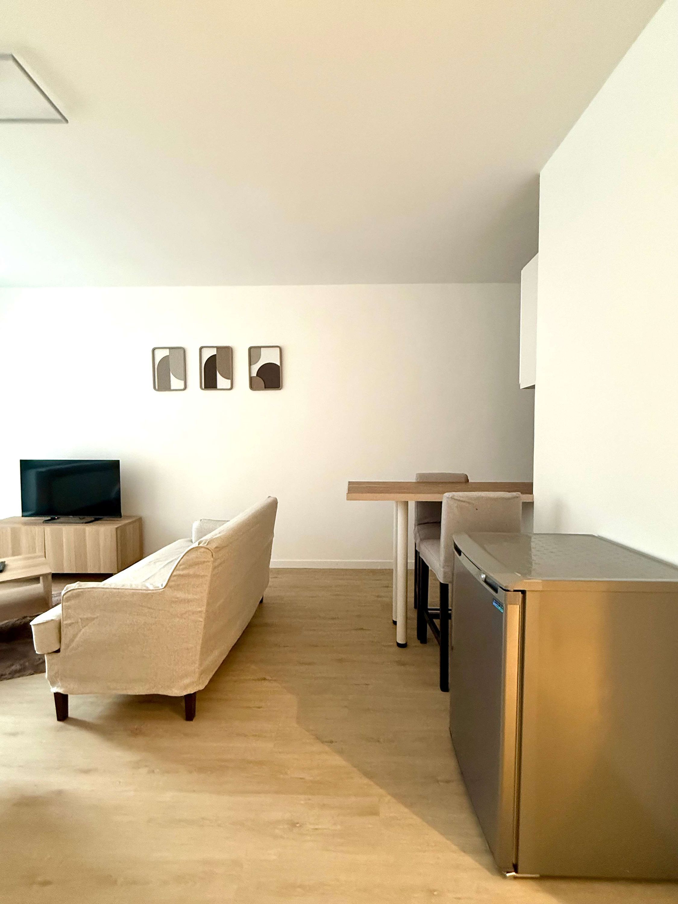 Um espaço de estar moderno e minimalista com um sofá, uma TV, uma mesa de jantar e um refrigerador.